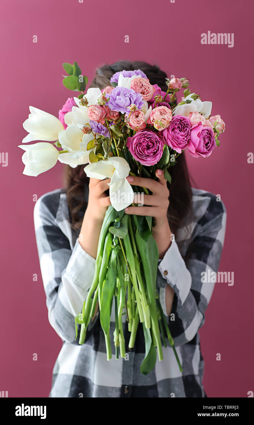 Beautiful young woman hiding face behind bouquet of flowers on color ...