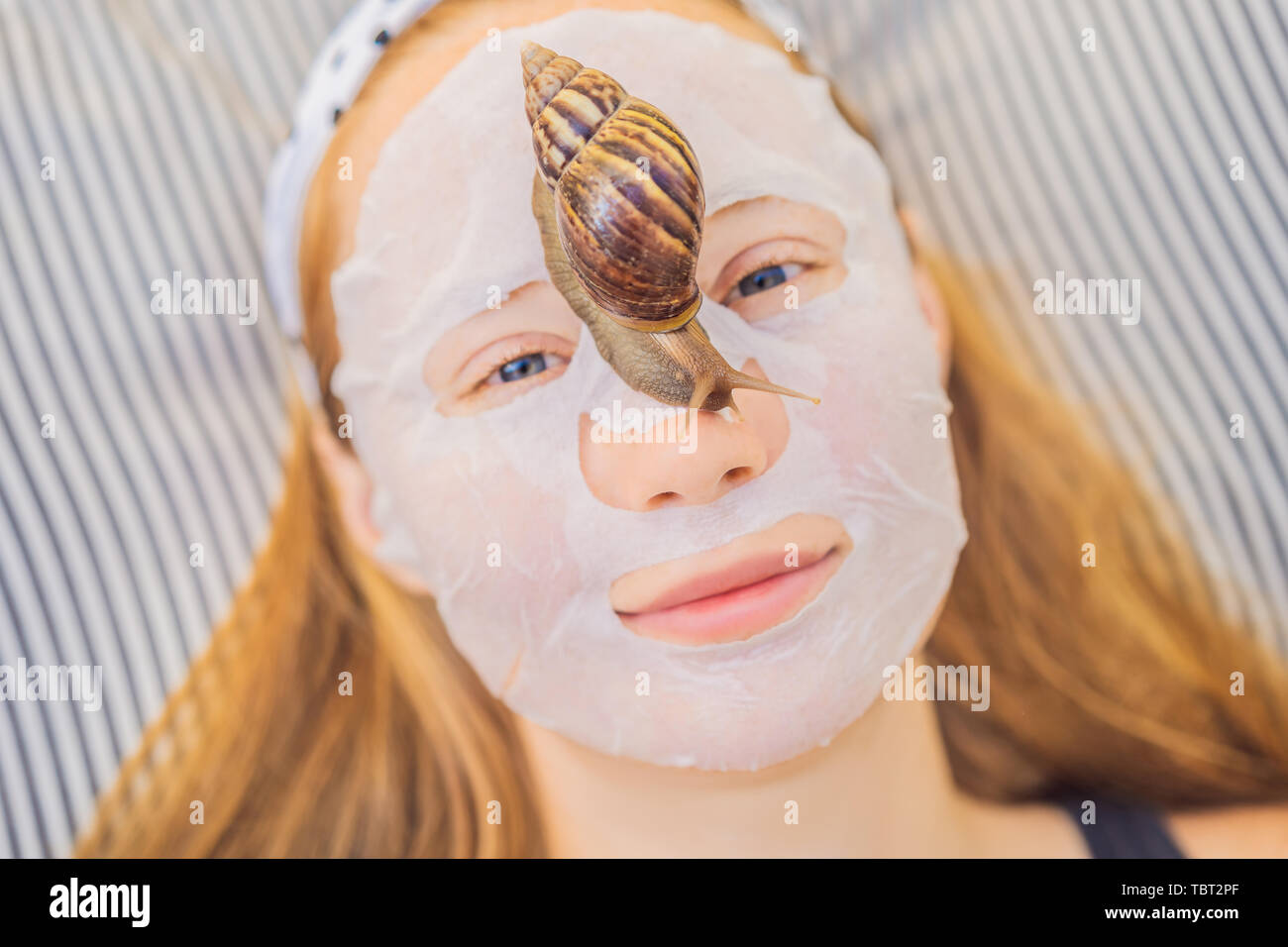 Young woman makes a face mask with snail mucus. Snail crawling on a ...