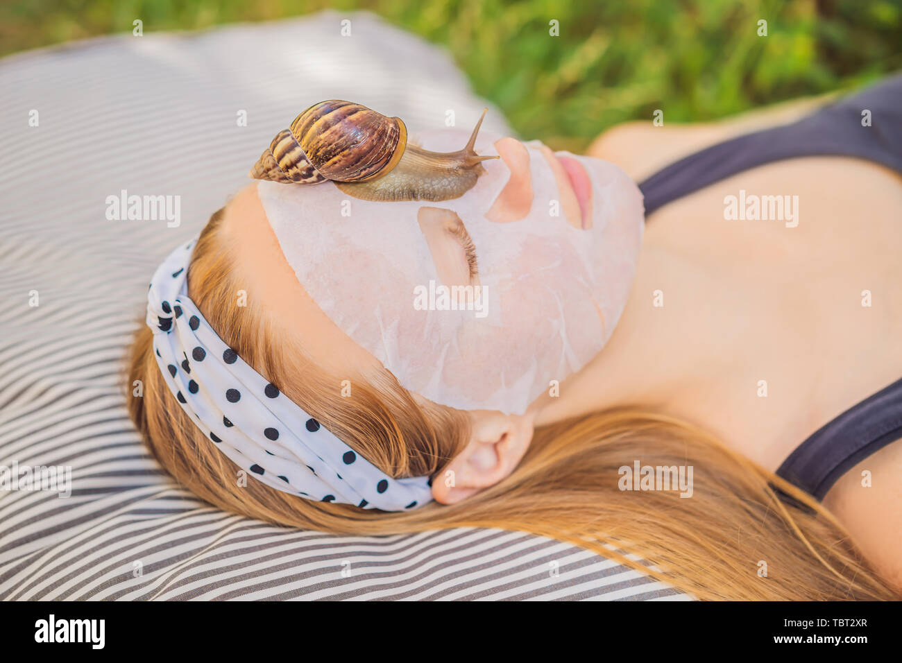Young woman makes a face mask with snail mucus. Snail crawling on a ...
