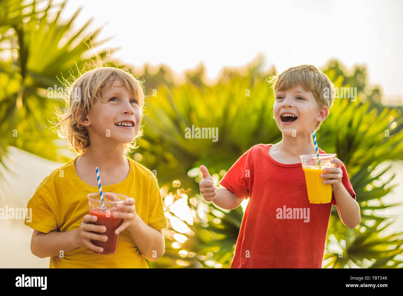 Two boys drink healthy smoothies against the backdrop of palm trees ...