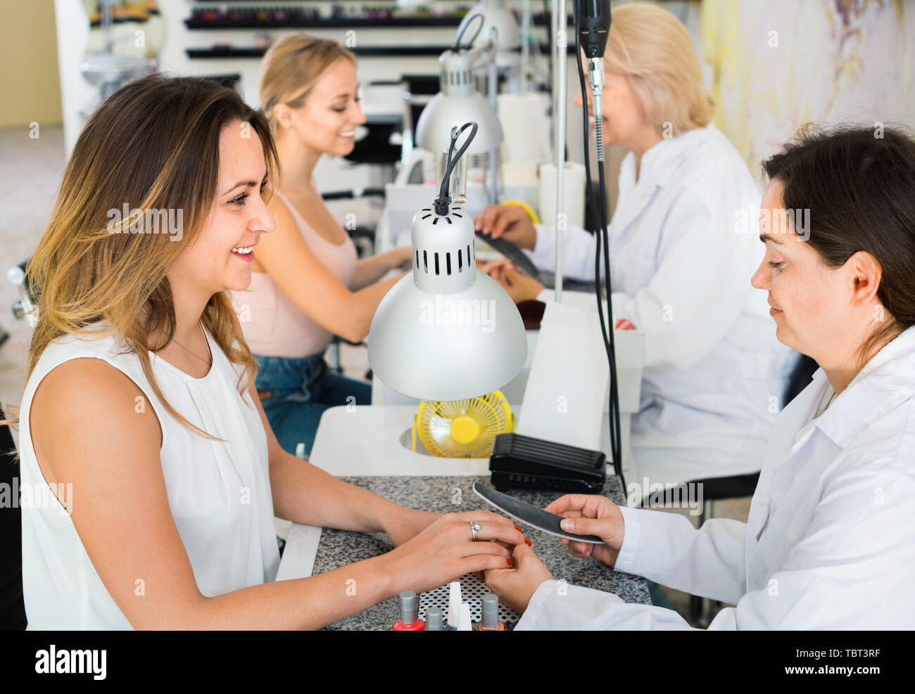 Two happy smiling women clients having manicure done in nail salon ...