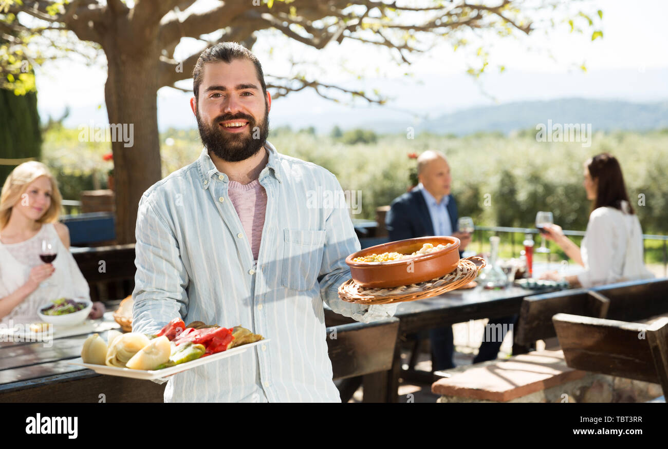 Portrait of smiling bearded waiter of rustic restaurant holding tray ...