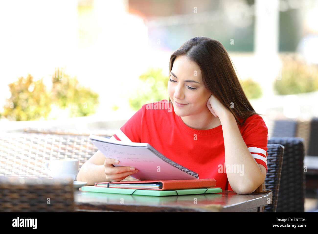Satisfied student in red studying reading notes sitting in a bar ...