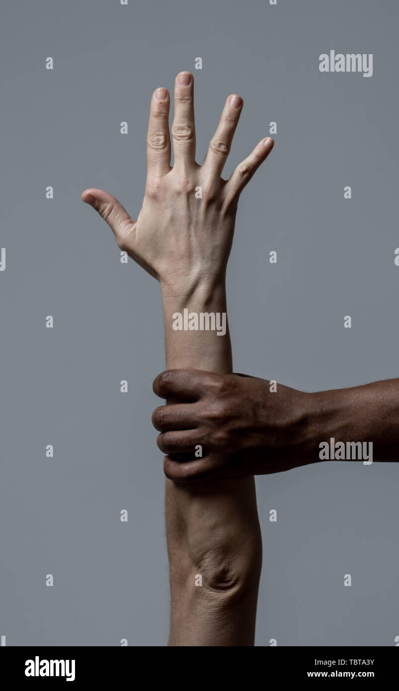 Black African American hand holding white skin arm. Conceptual image of ...
