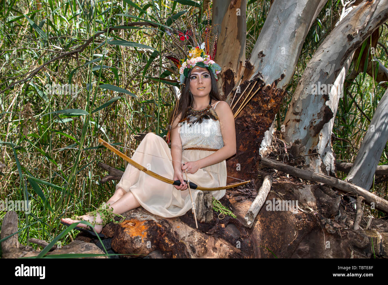 A girl in a Pocahontas dress with a bow and arrow sits in the thickets ...