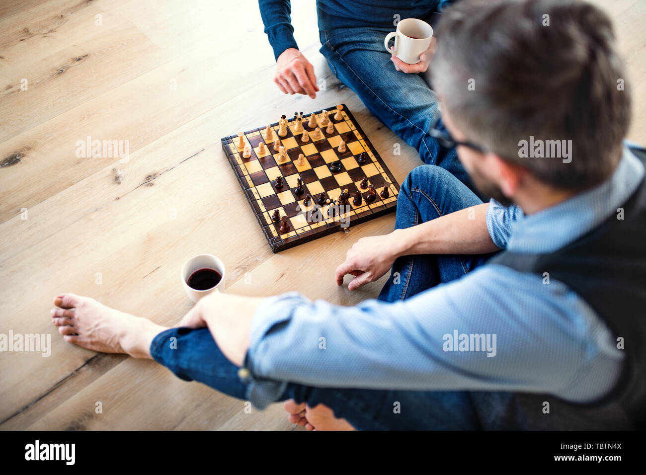 A midsection of adult son and senior father sitting on floor indoors ...