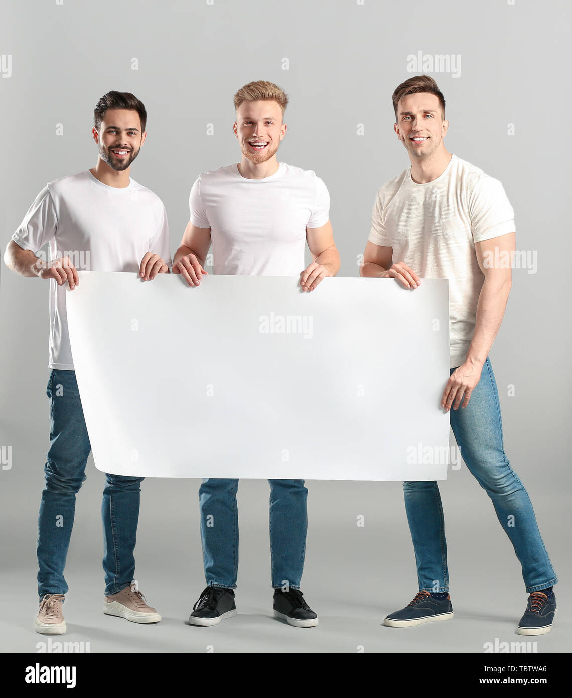 Handsome young men with empty poster on grey background Stock Photo - Alamy