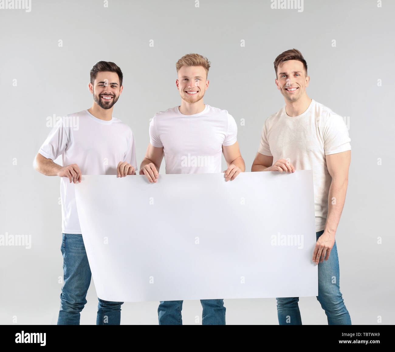 Handsome young men with empty poster on grey background Stock Photo - Alamy