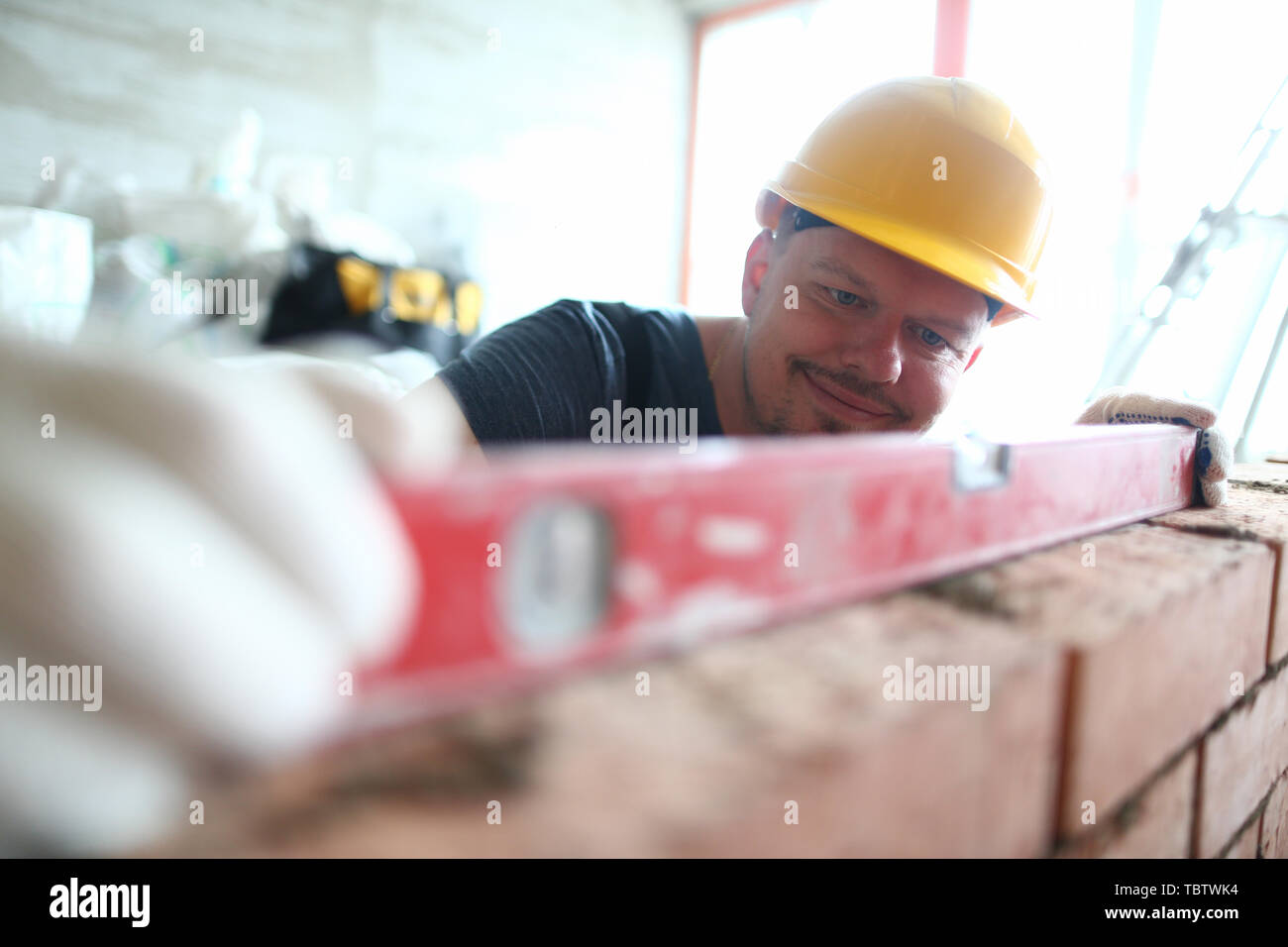 Portrait of pedantic male using special tool to measure height of brick wall. Bearded builder ...