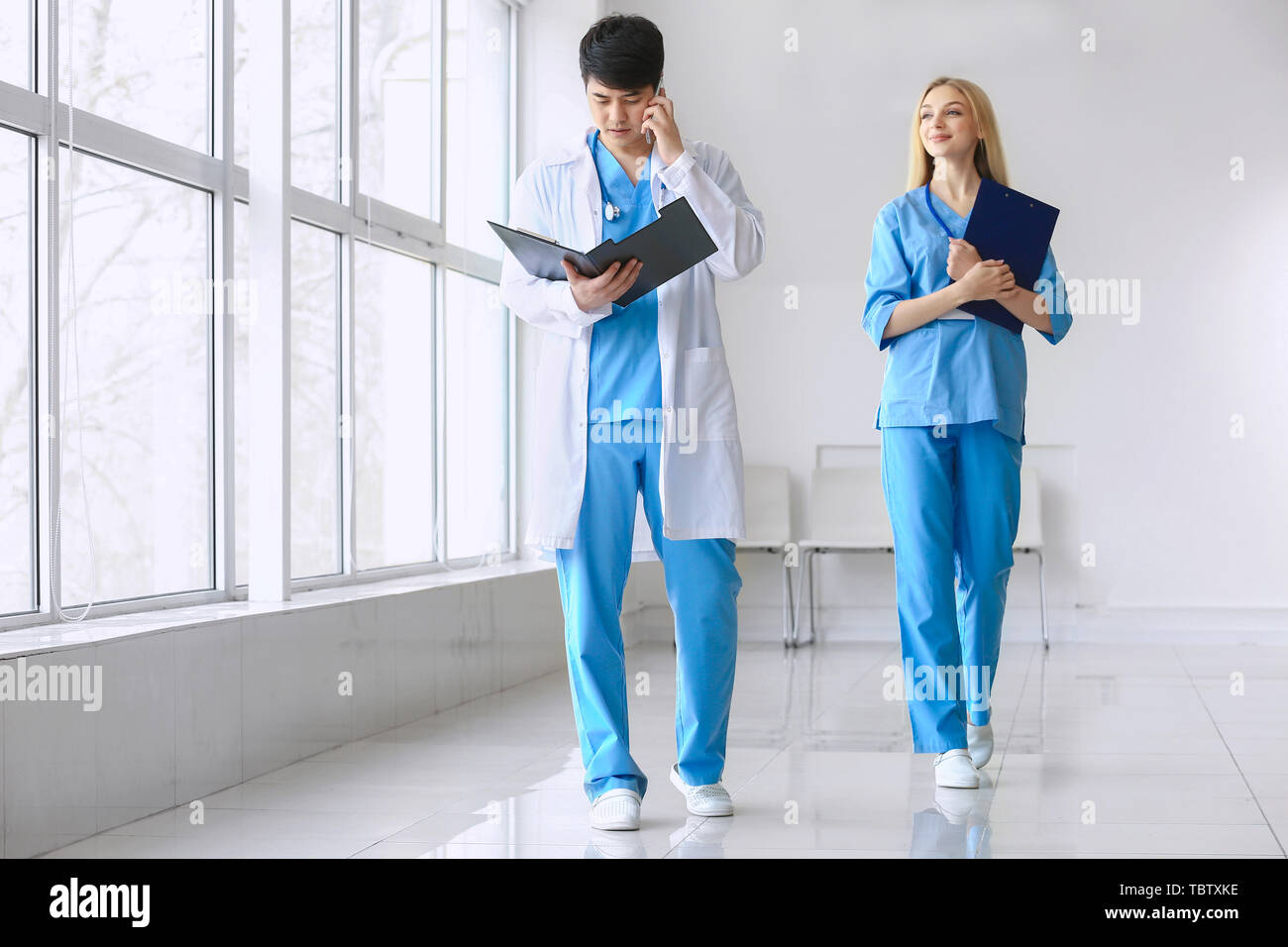 Male doctor and female medical assistant walking down the corridor in ...