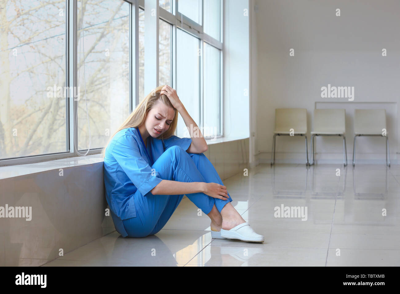 Depressed female medical assistant sitting near window in clinic Stock ...