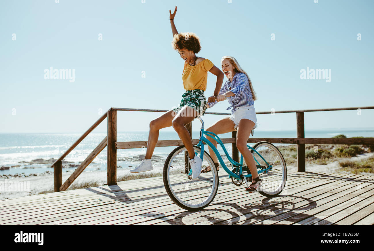 Cheerful young women taking a bike ride together at the beach. Female ...