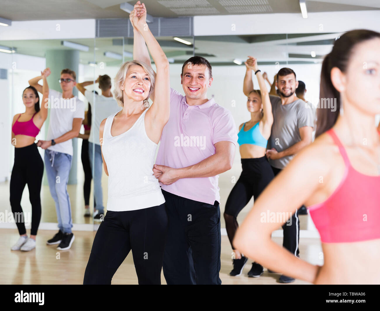 happy greek men and women of different ages dancing salsa in dance hall ...