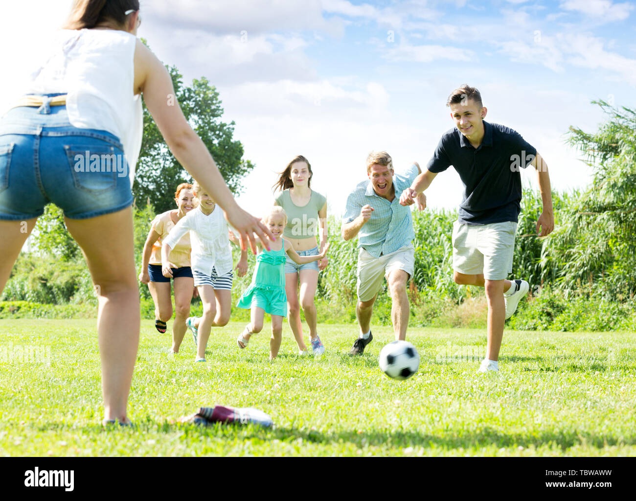 Positive parents with four kids playing soccer together on green field ...