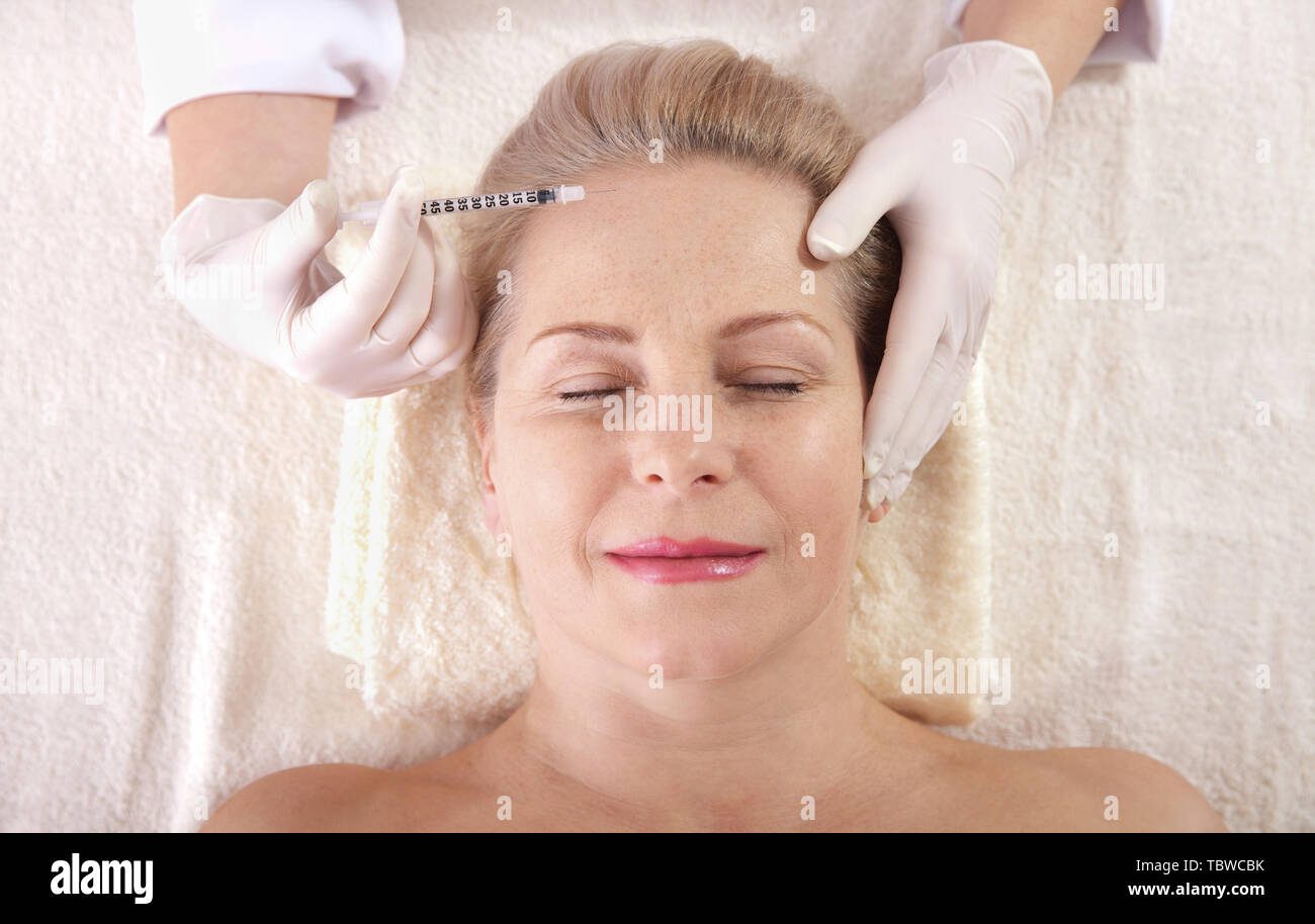Middle aged woman gets cosmetic injection in her forehead. Hyaluronic ...