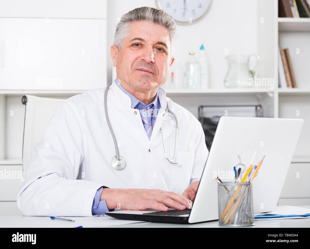 Doctor in white gown behind desk and computer at hospital office Stock ...