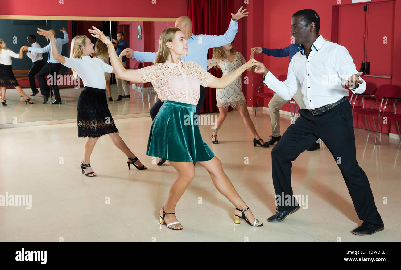 Young smiling people practicing vigorous jive movements in dance class ...