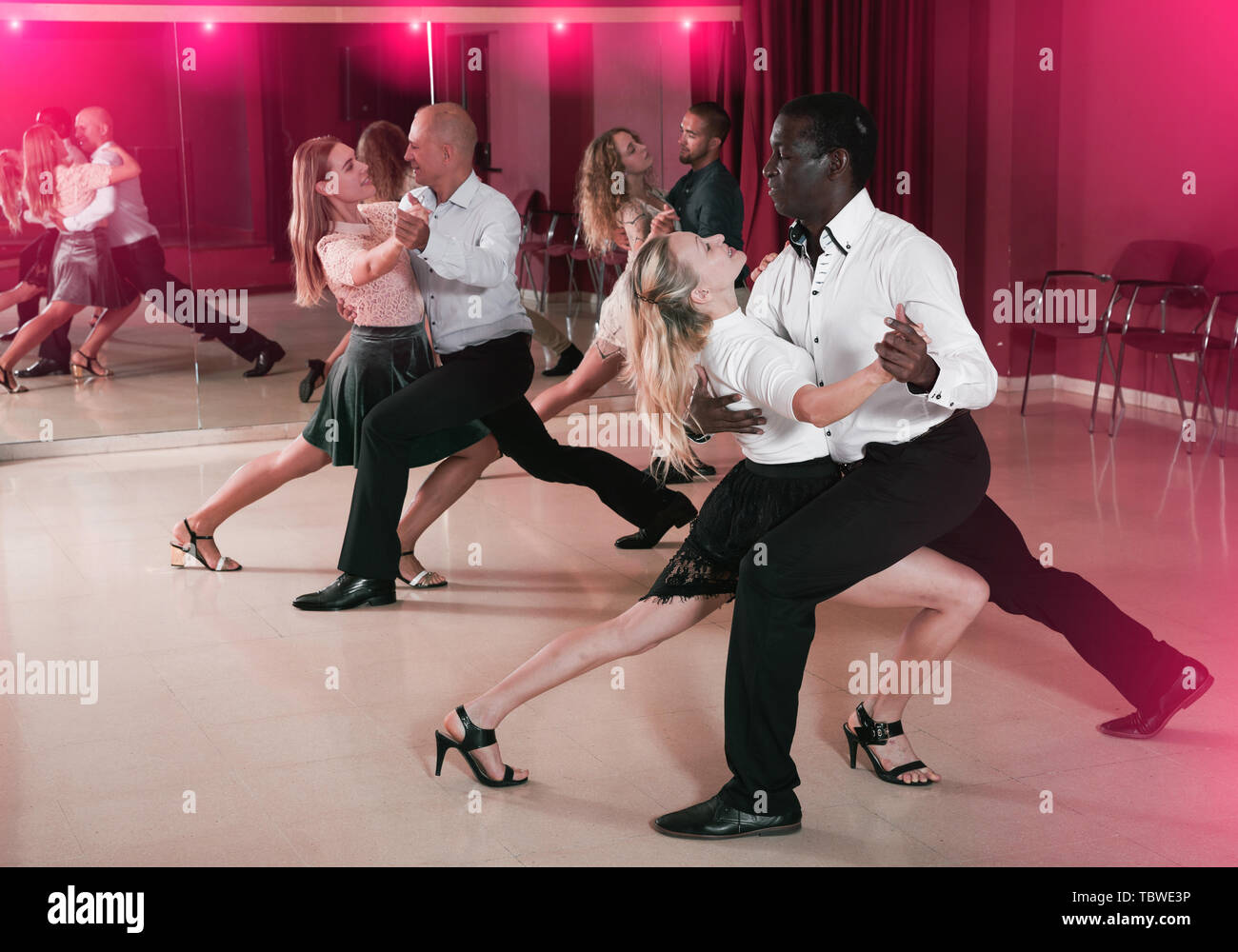 Smiling adult pairs dancing tango movements in modern dance studio ...