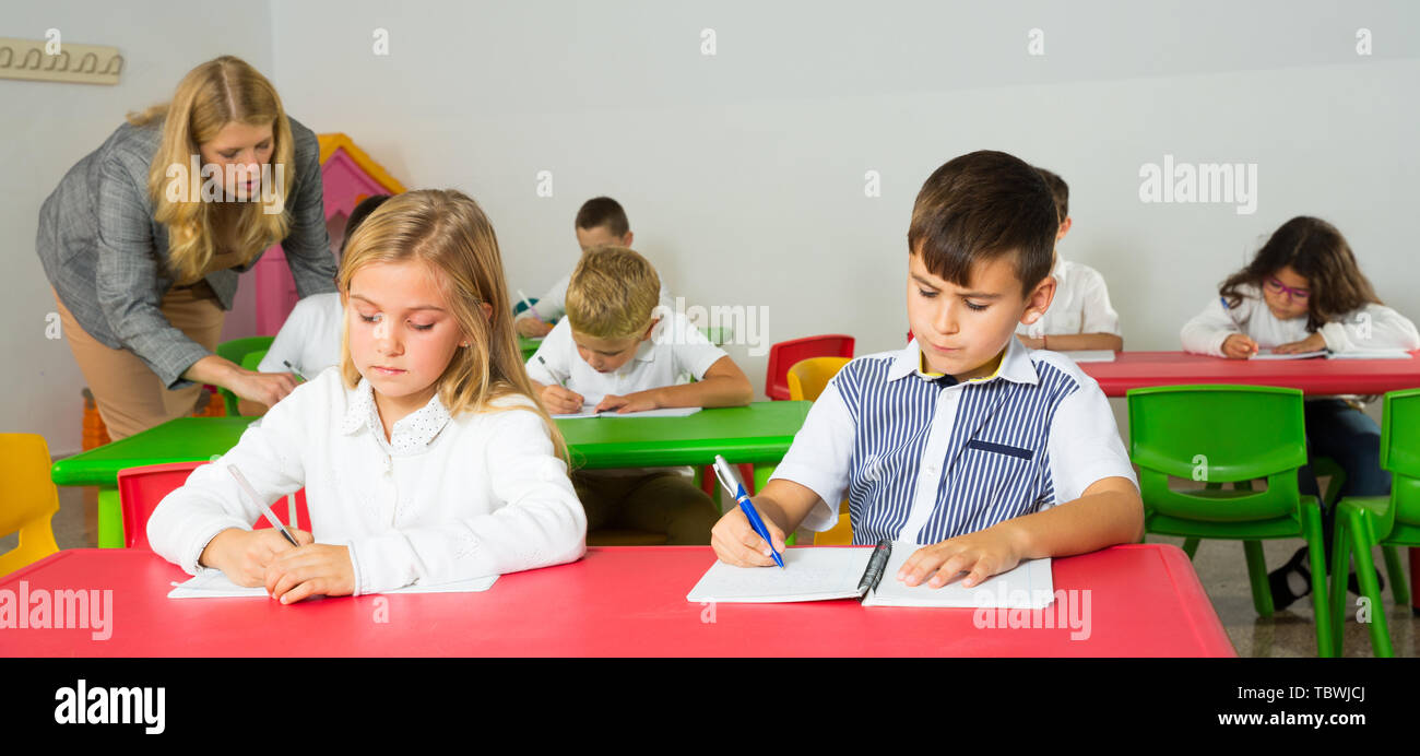 Female teacher helping schoolchildren doing their task in classroom ...