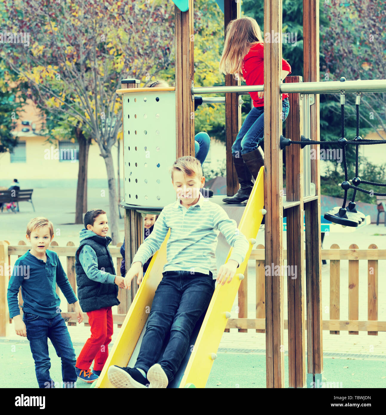 Smiling glad children in school age sliding down together on playground ...
