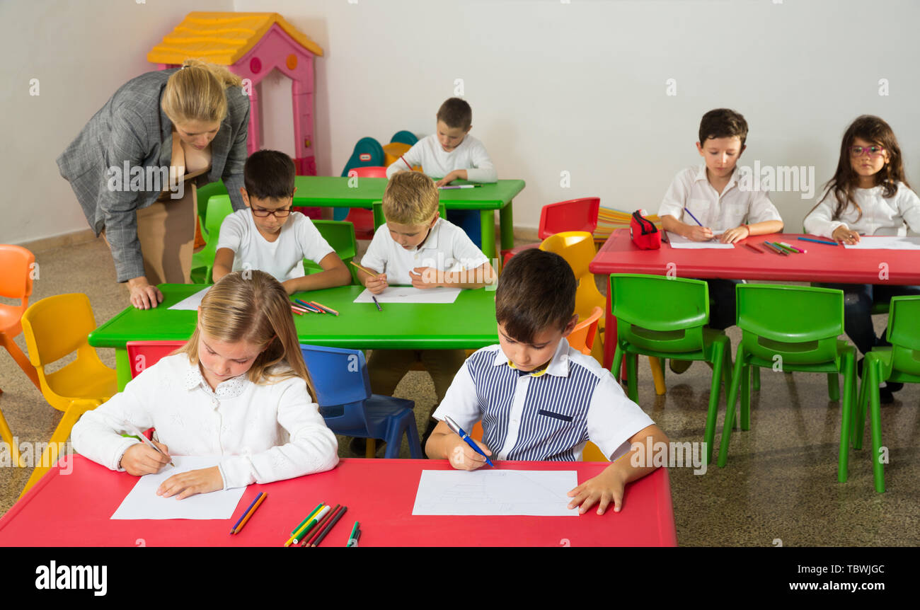 Female teacher helping schoolchildren doing their task in classroom ...