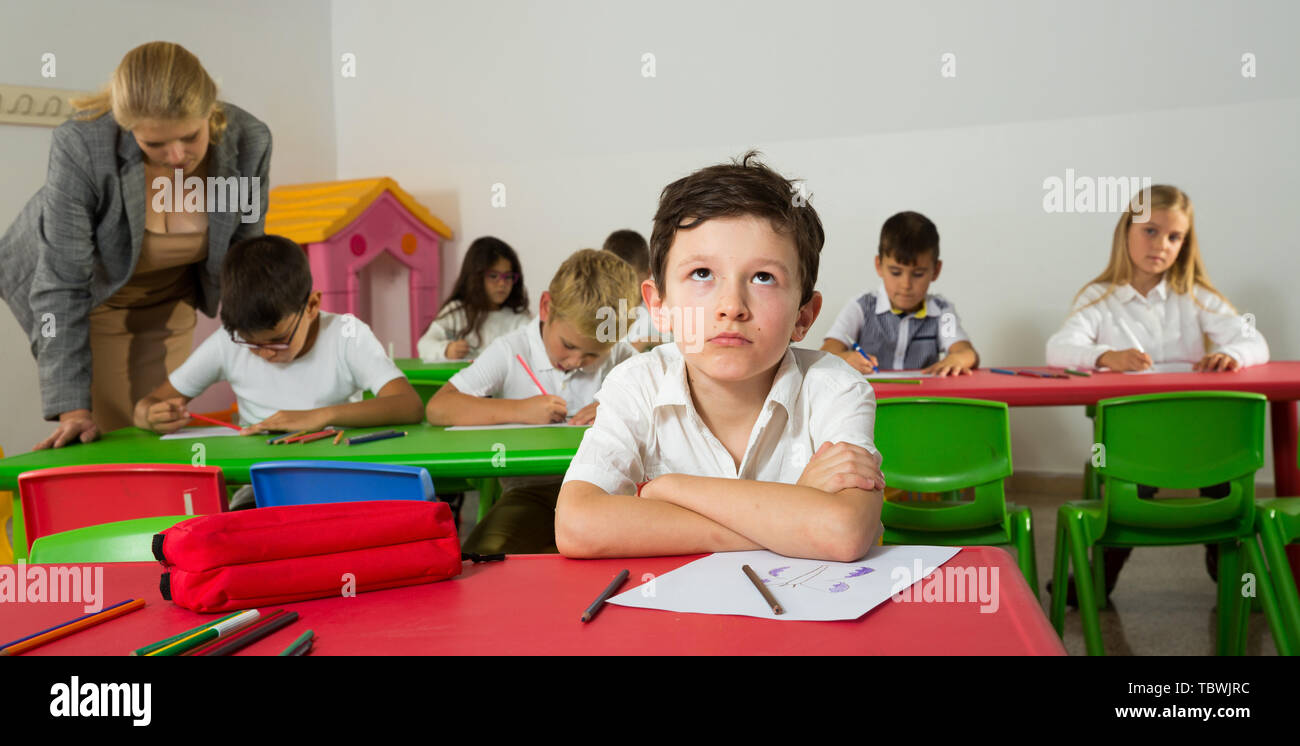 Portrait of bored schoolboy sitting in classroom with classmates and ...