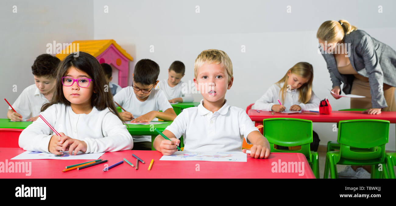 Happy cheerful smiling female teacher helping schoolkids drawing with ...