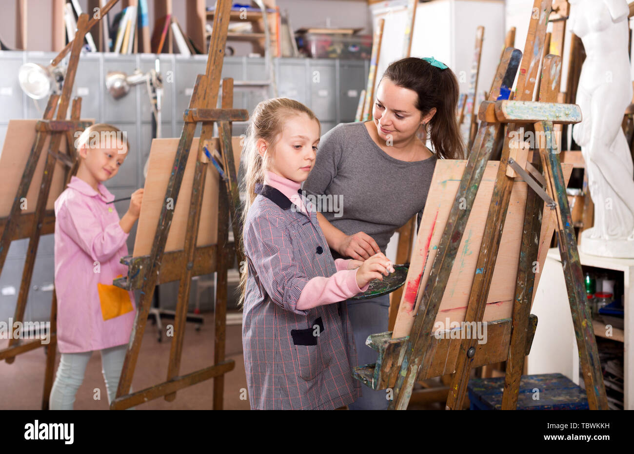 Glad young female teacher helping girl during painting class at art ...