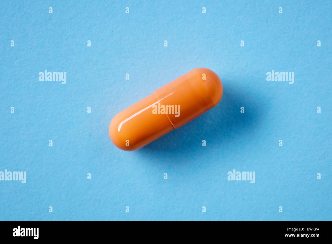Macro view of orange colored medical pill capsule on blue background ...
