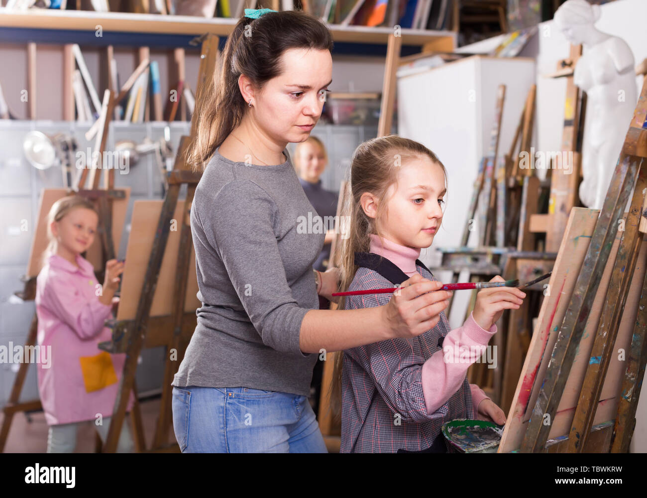 Smiling female teacher assisting student during painting class at ...