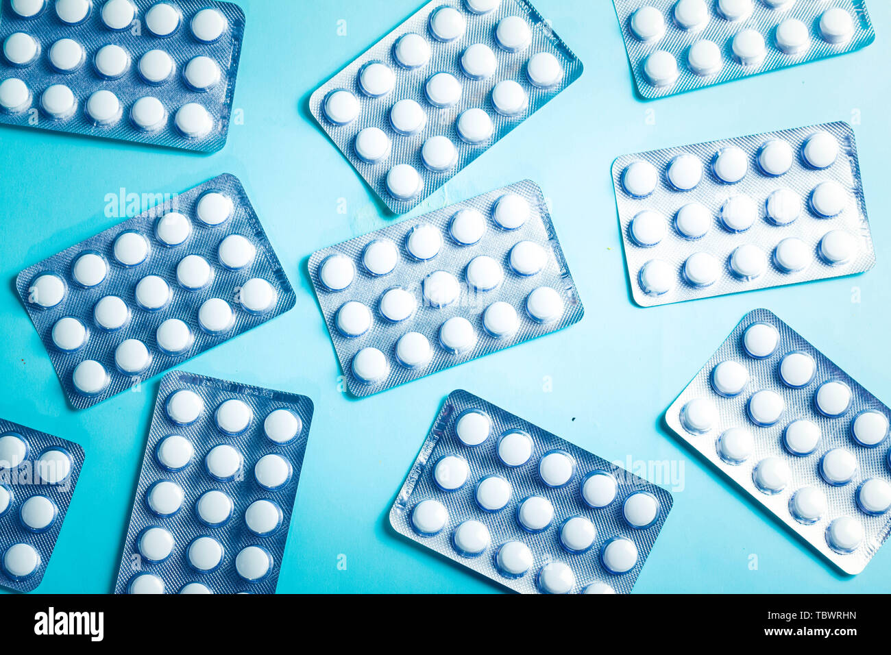 Pile of medical white pills packages on blue background top view, toned ...