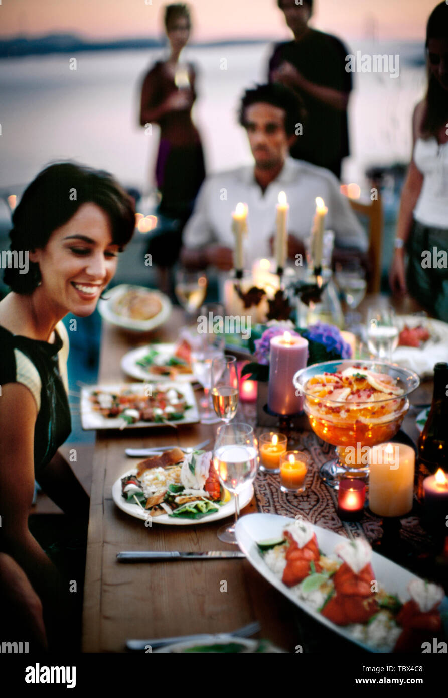 Smiling young woman looking down at her plate while seated around an ...