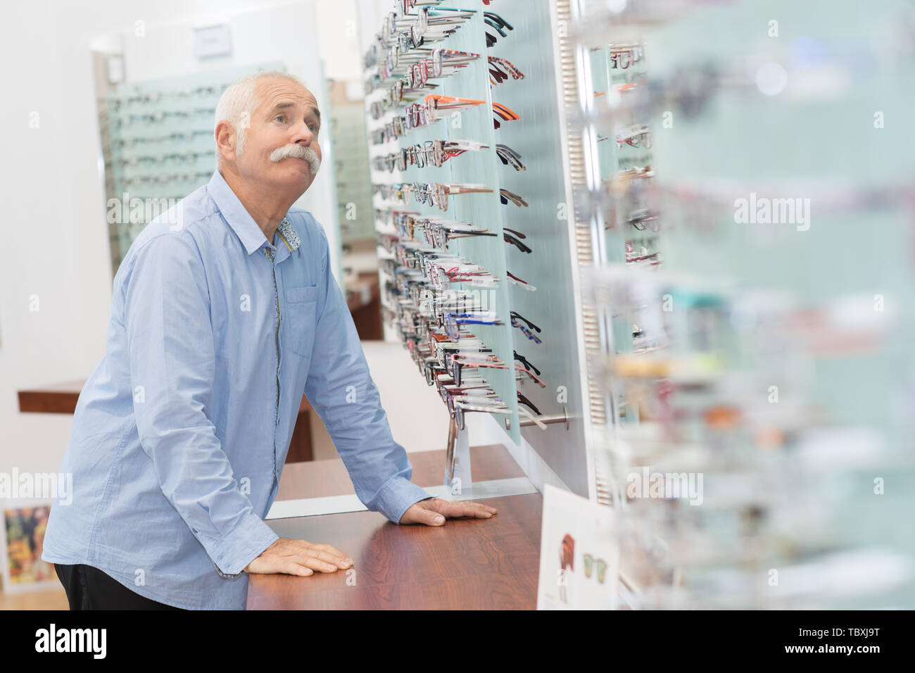 indecisive senior man looking at display of eyeglasses in opticians ...
