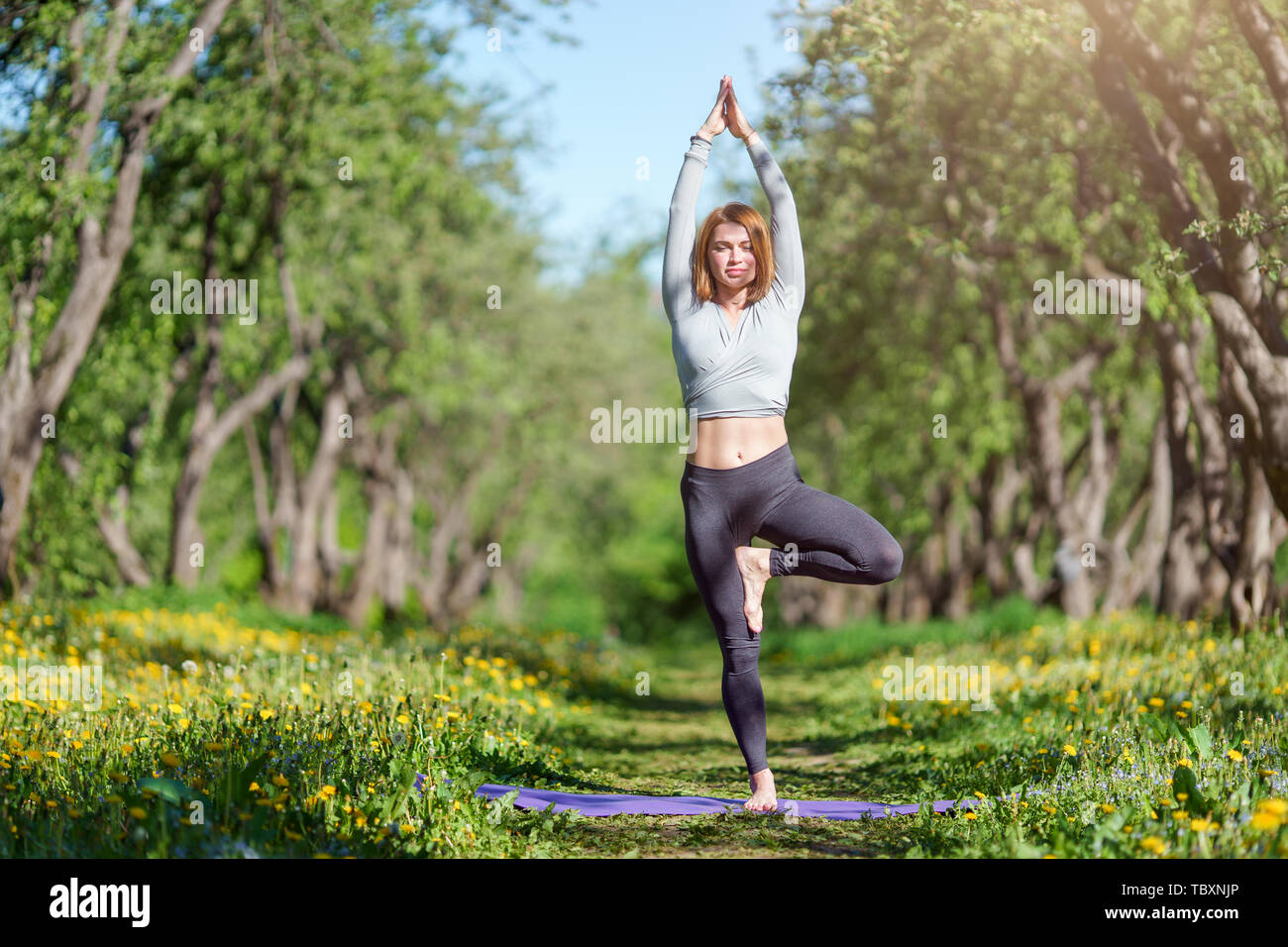 Image of woman with one arm raised on one leg practicing yoga in forest ...