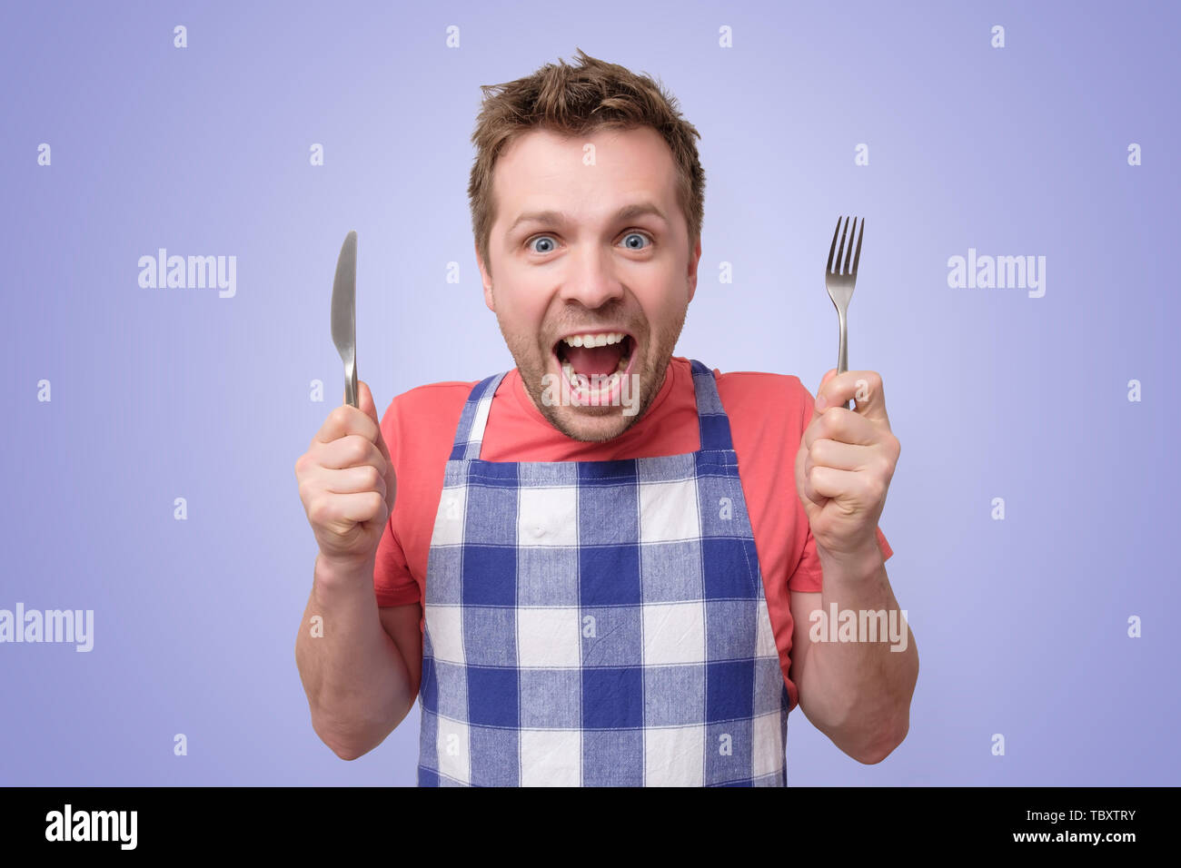 Man in apron holding cutlery fork and knife Stock Photo - Alamy