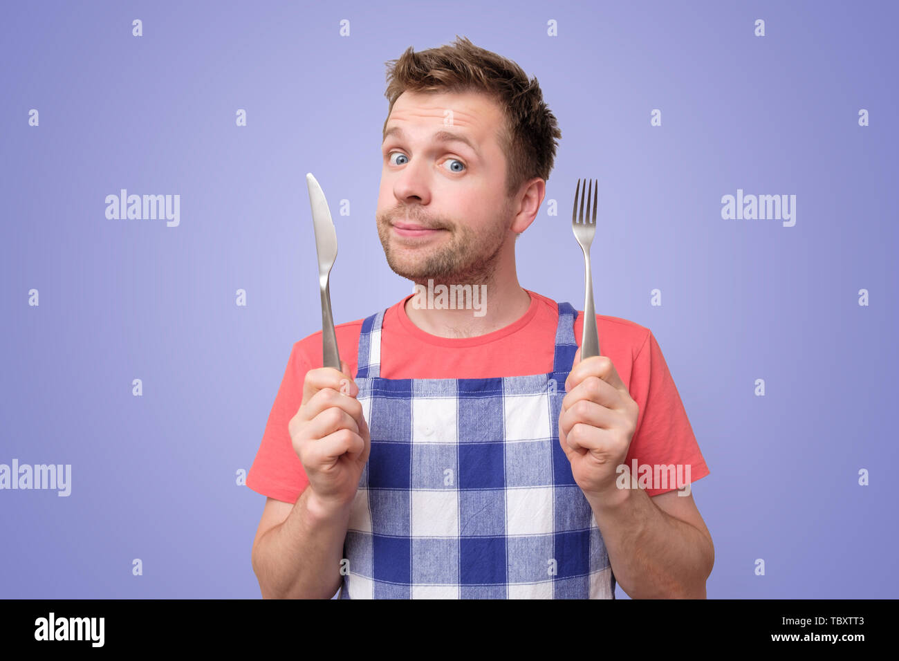 Man in apron holding cutlery fork and knife Stock Photo - Alamy