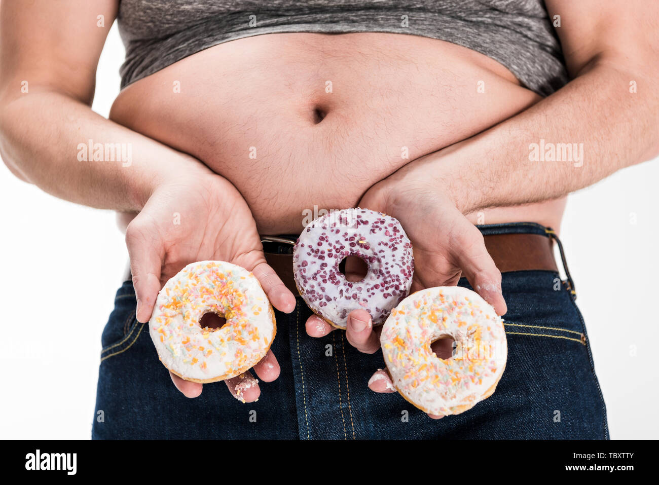 cropped view of overweight man showing belly and holding donuts ...
