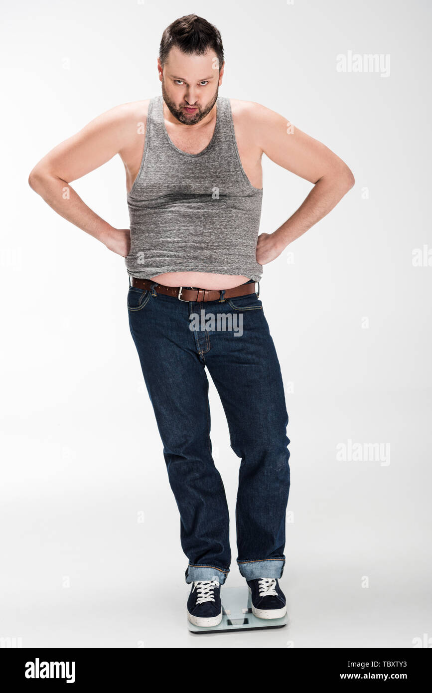 angry overweight man with hands akimbo standing on electronic weight ...