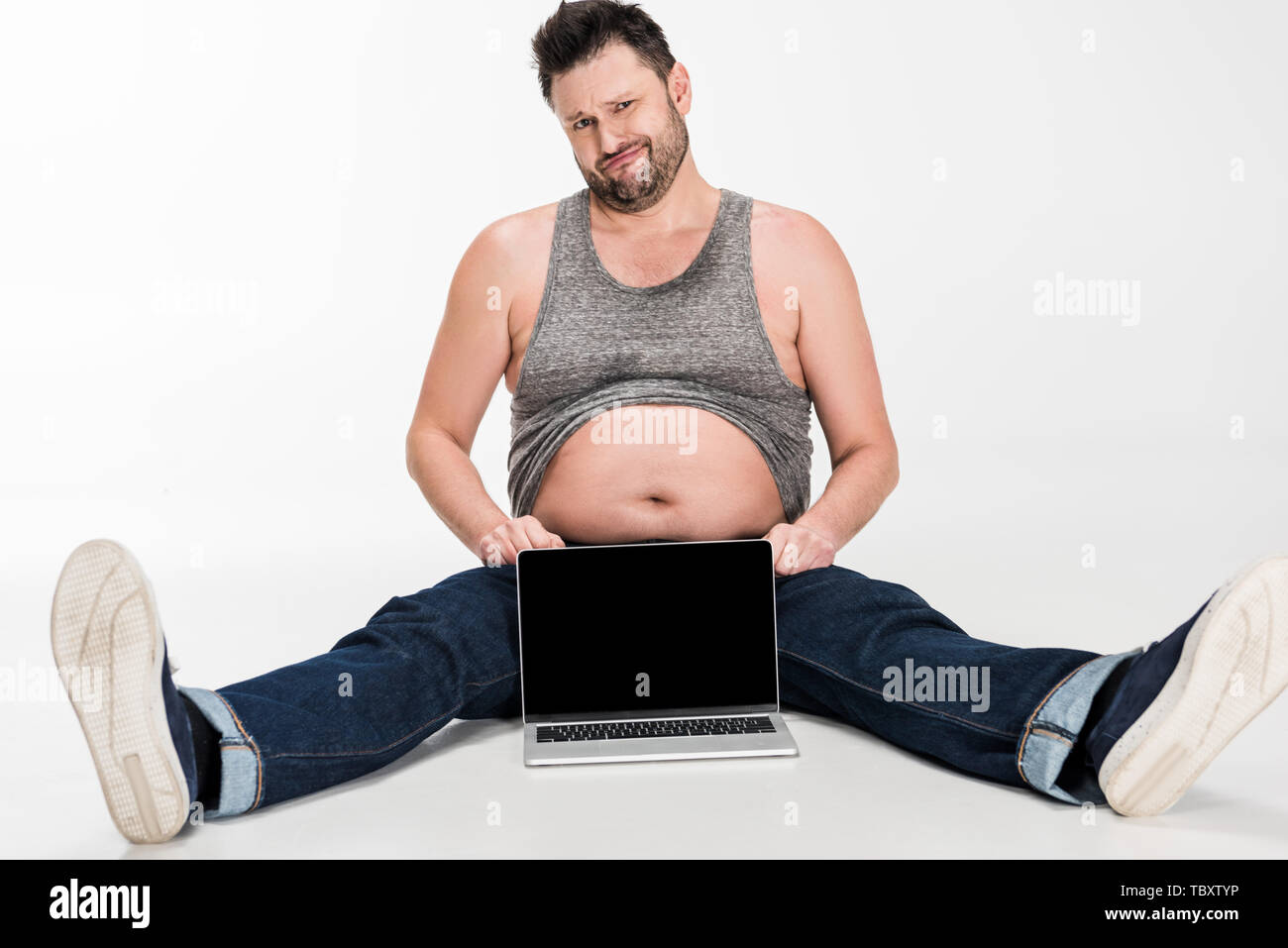 skeptical overweight man looking at camera while sitting near laptop ...
