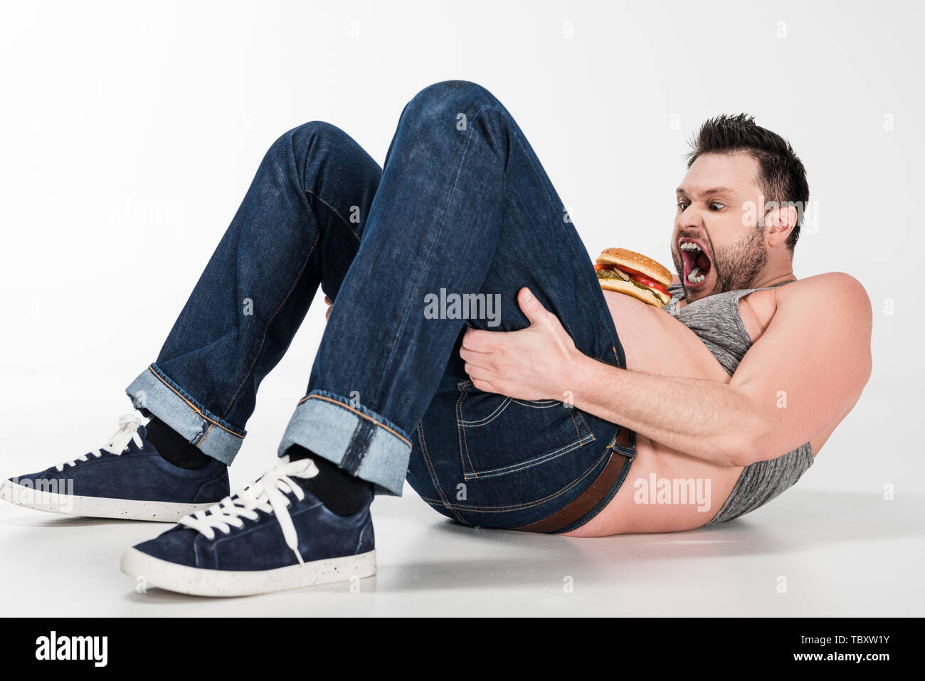 angry overweight man with burger on belly lying and doing abs exercise ...