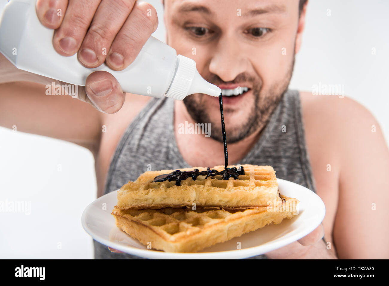 close up view of chubby man pouring chocolate syrup on waffles isolated ...