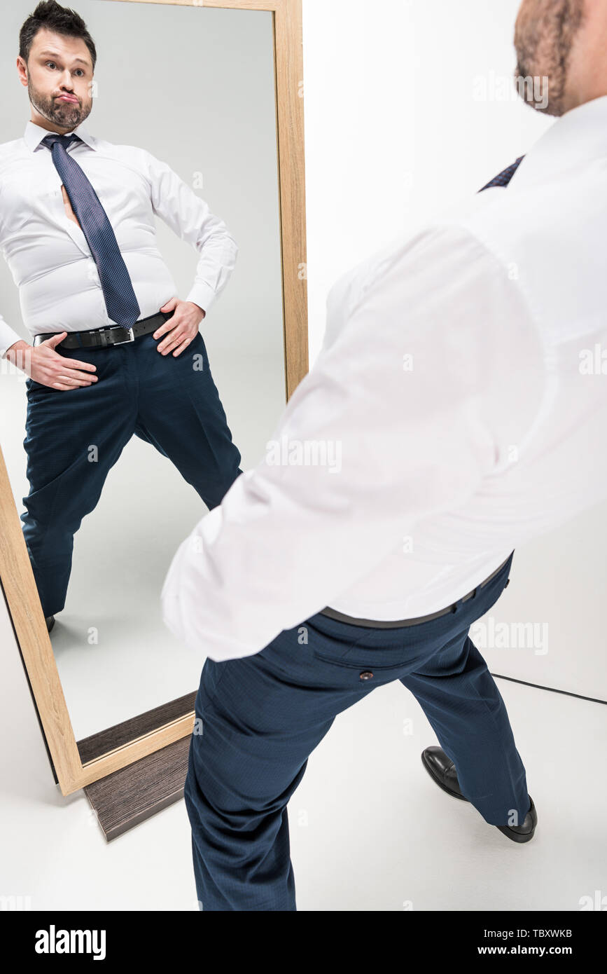 overweight man in formal wear looking at reflection in mirror and ...