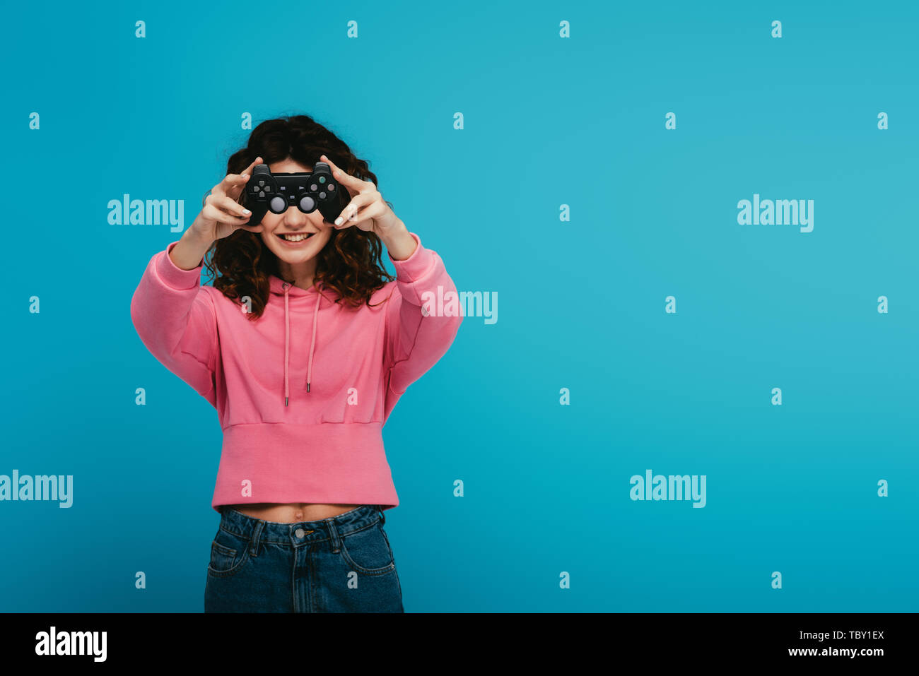 Happy Curly Redhead Girl Covering Face With Joystick On Blue Stock 8575