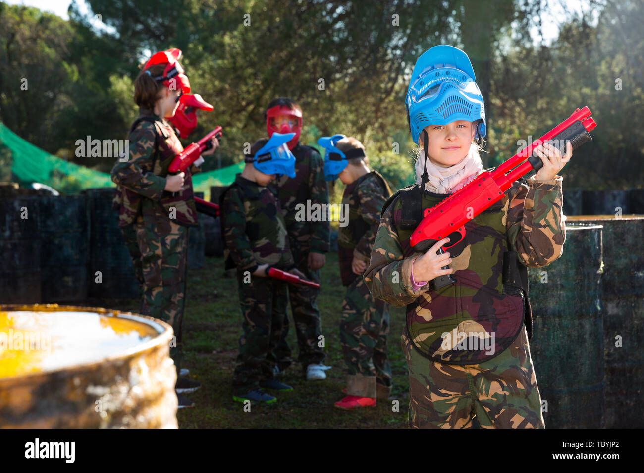 portrait of little girl paintball player in camouflage standing with ...