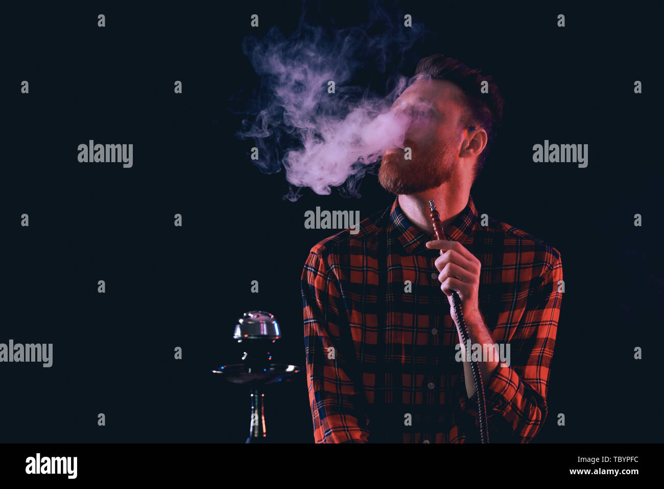 Young man smoking hookah on dark background Stock Photo - Alamy