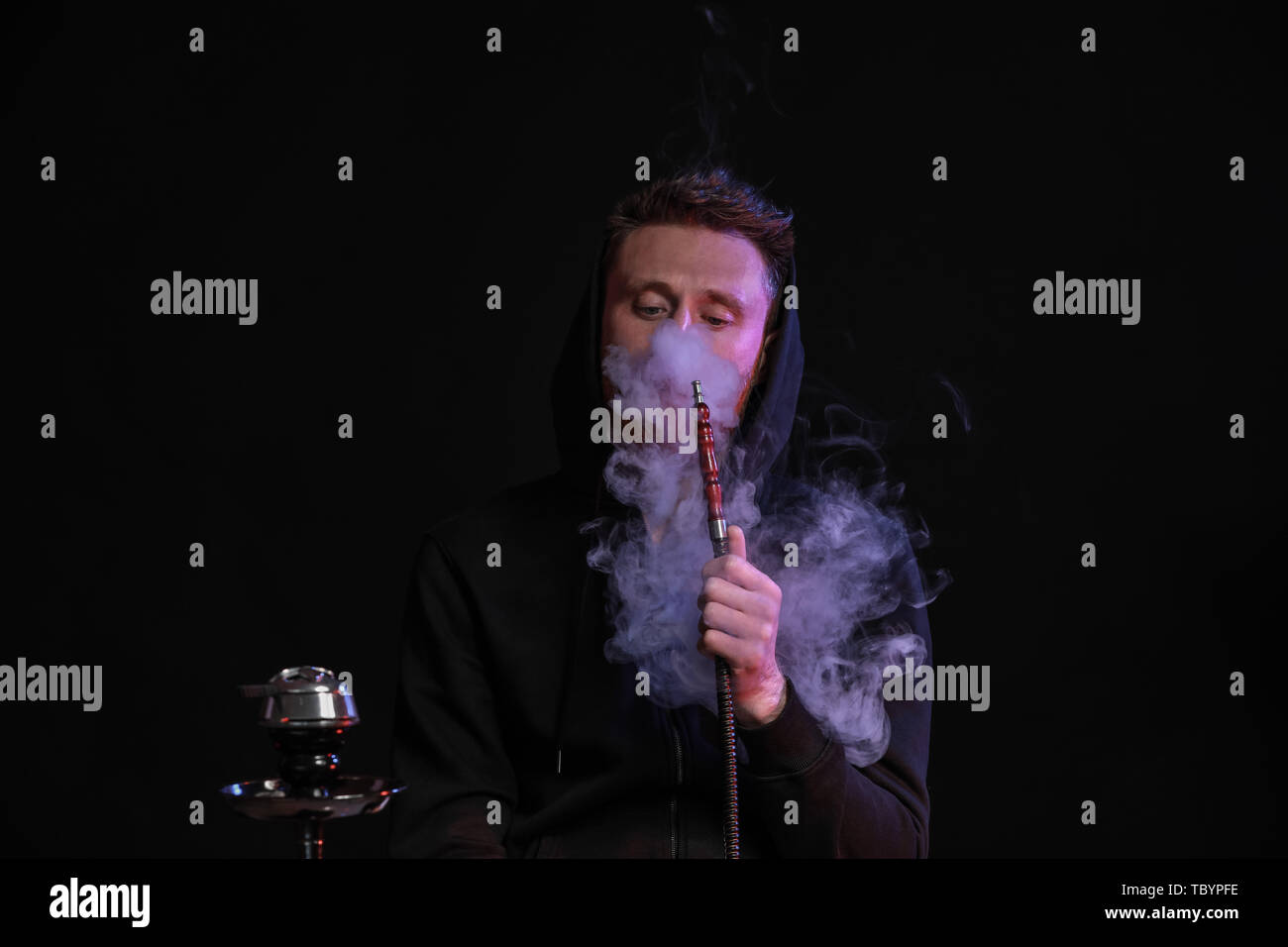 Young man smoking hookah on dark background Stock Photo - Alamy