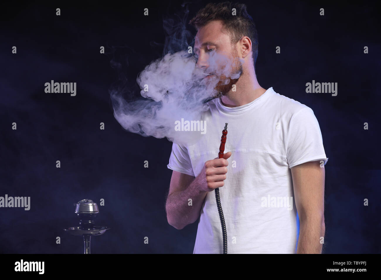 Young man smoking hookah on dark background Stock Photo - Alamy