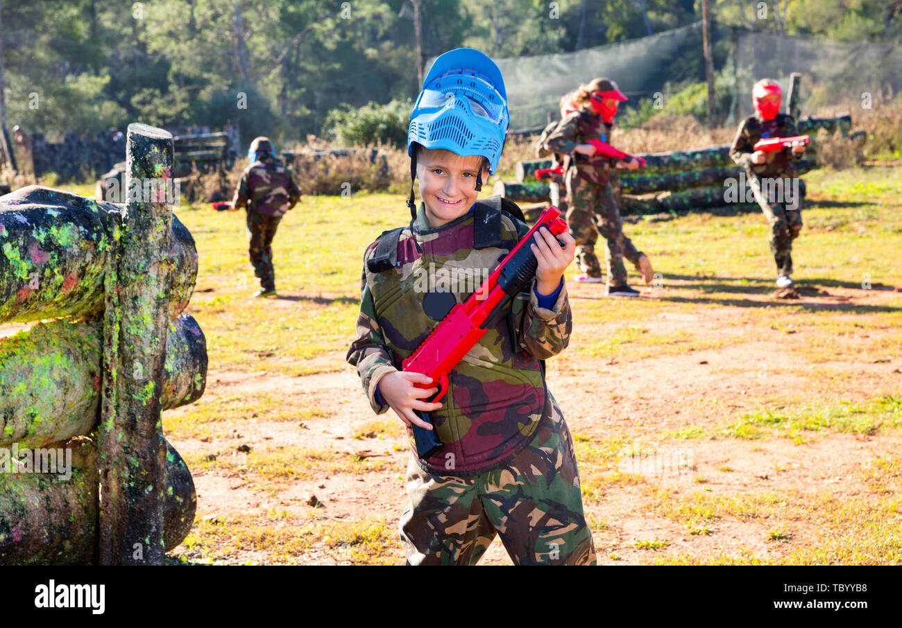Happy smiling boy paintball player in camouflage standing with gun ...