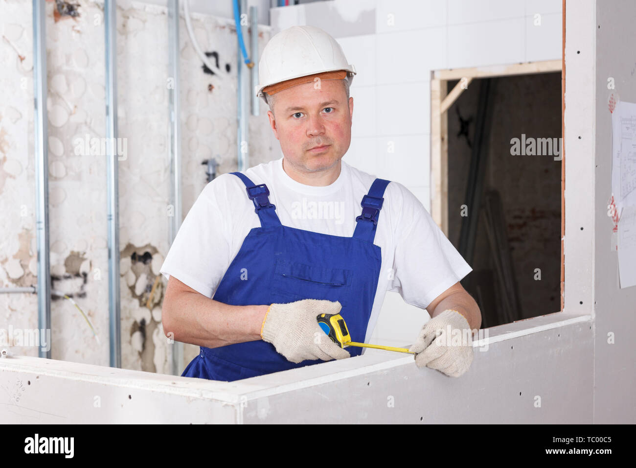 Confident builder measuring drywall dividing wall construction in ...