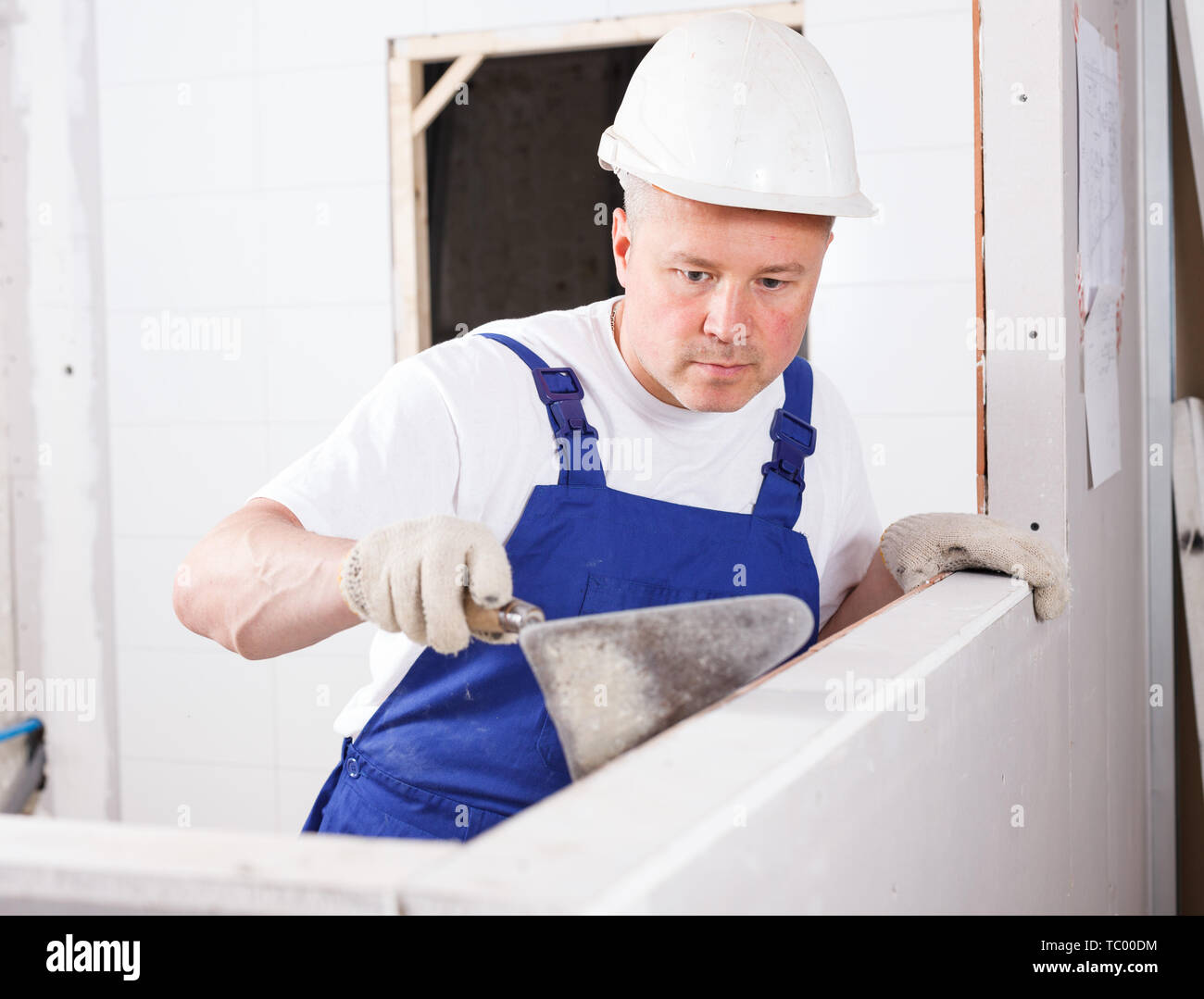 Confident builder filling gaps on drywall element with setting compound ...